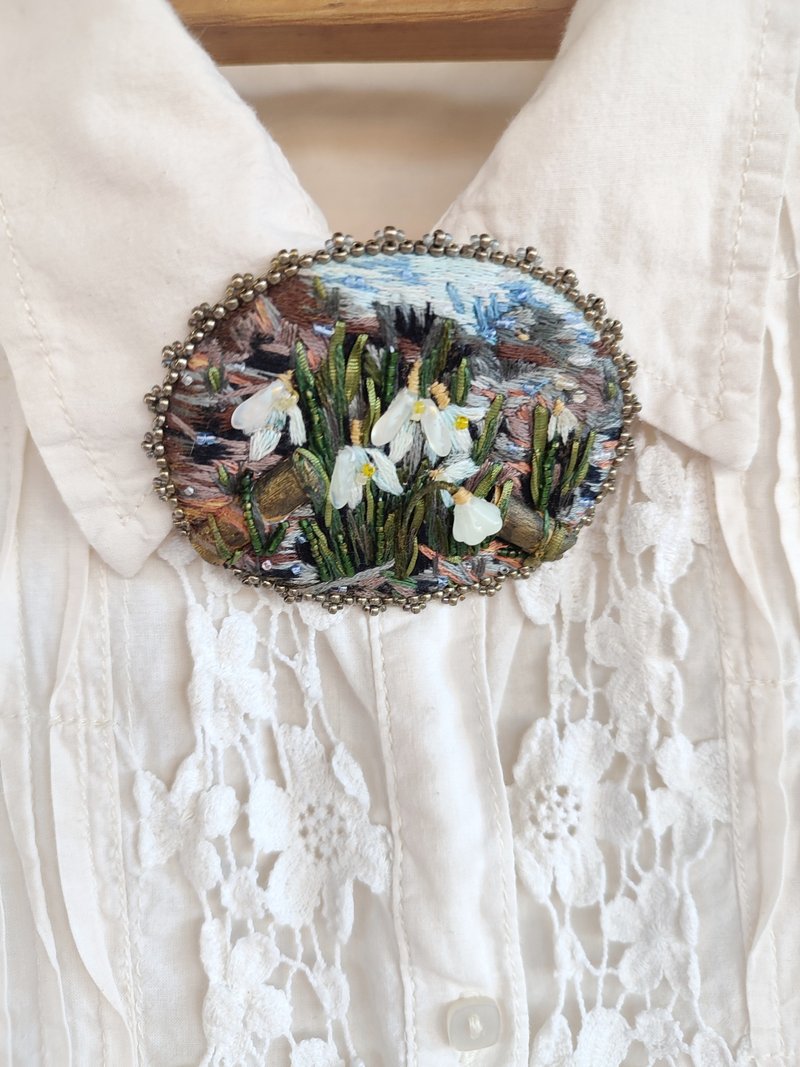 Round embroidered brooch with snowdrops in a forest clearing. With ...